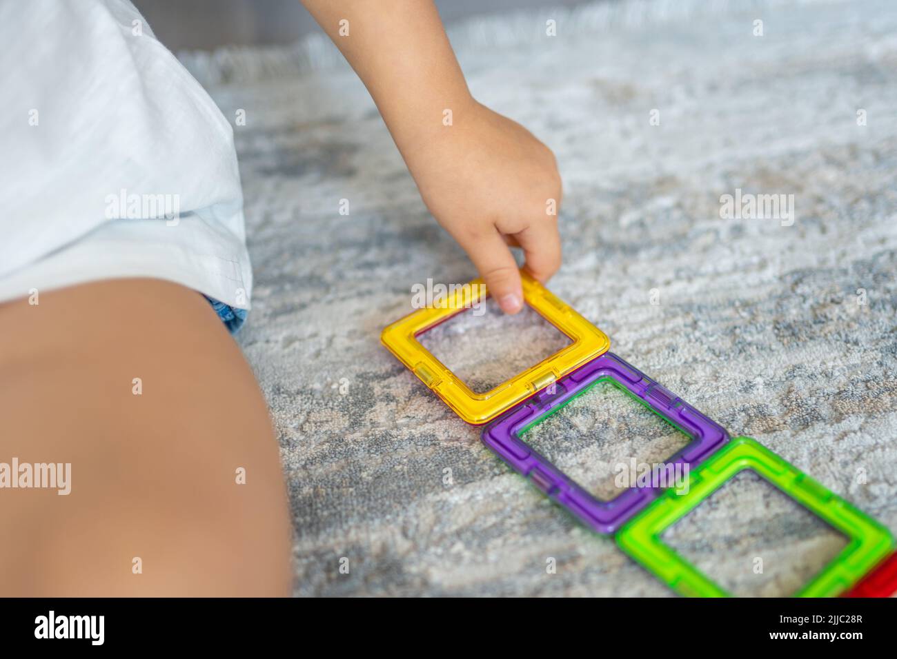 Little girl playing colorful magnet plastic blocks kit at home. The ...