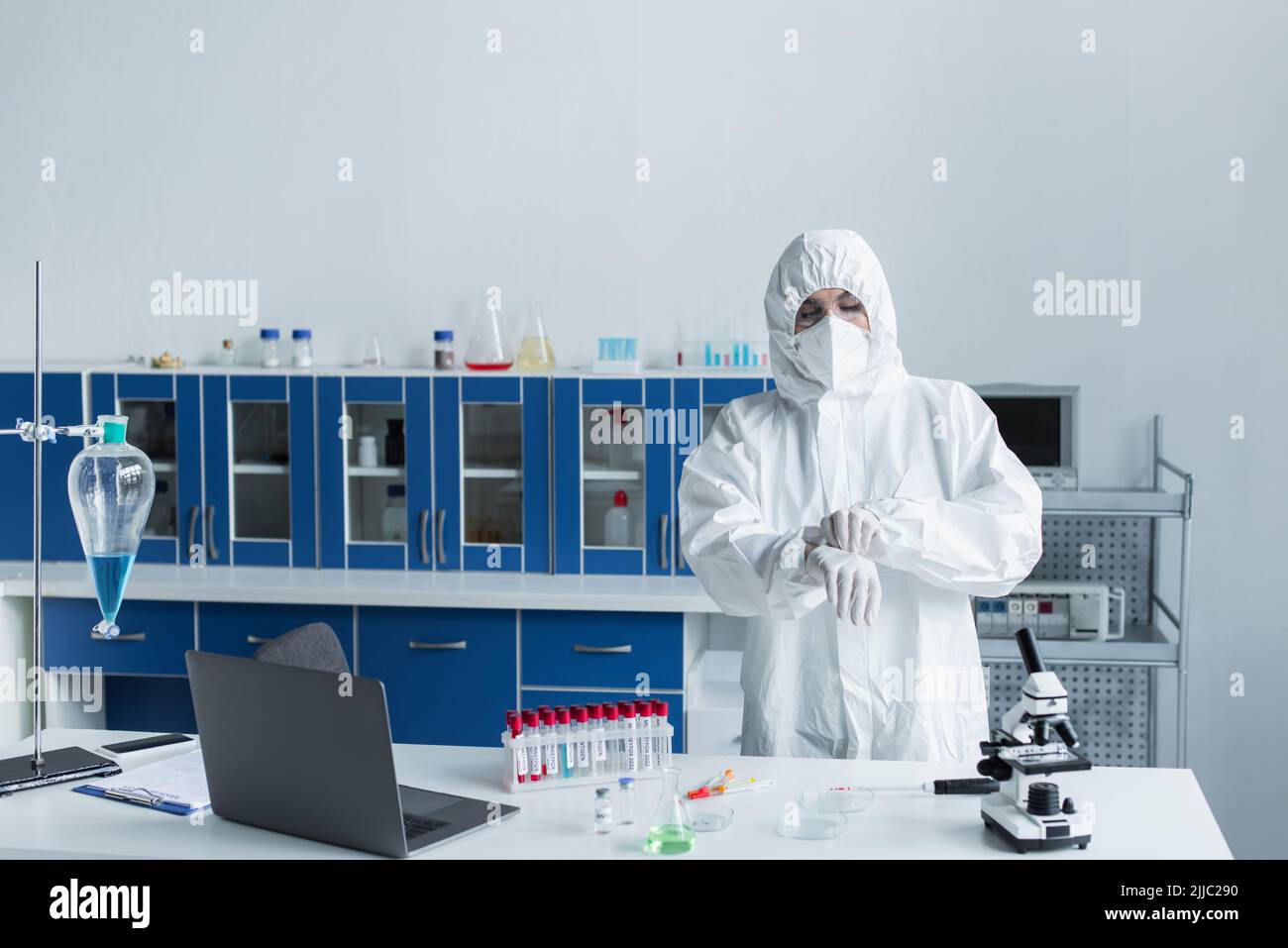 Scientist in hazmat suit and latex gloves standing near test tubes and ...