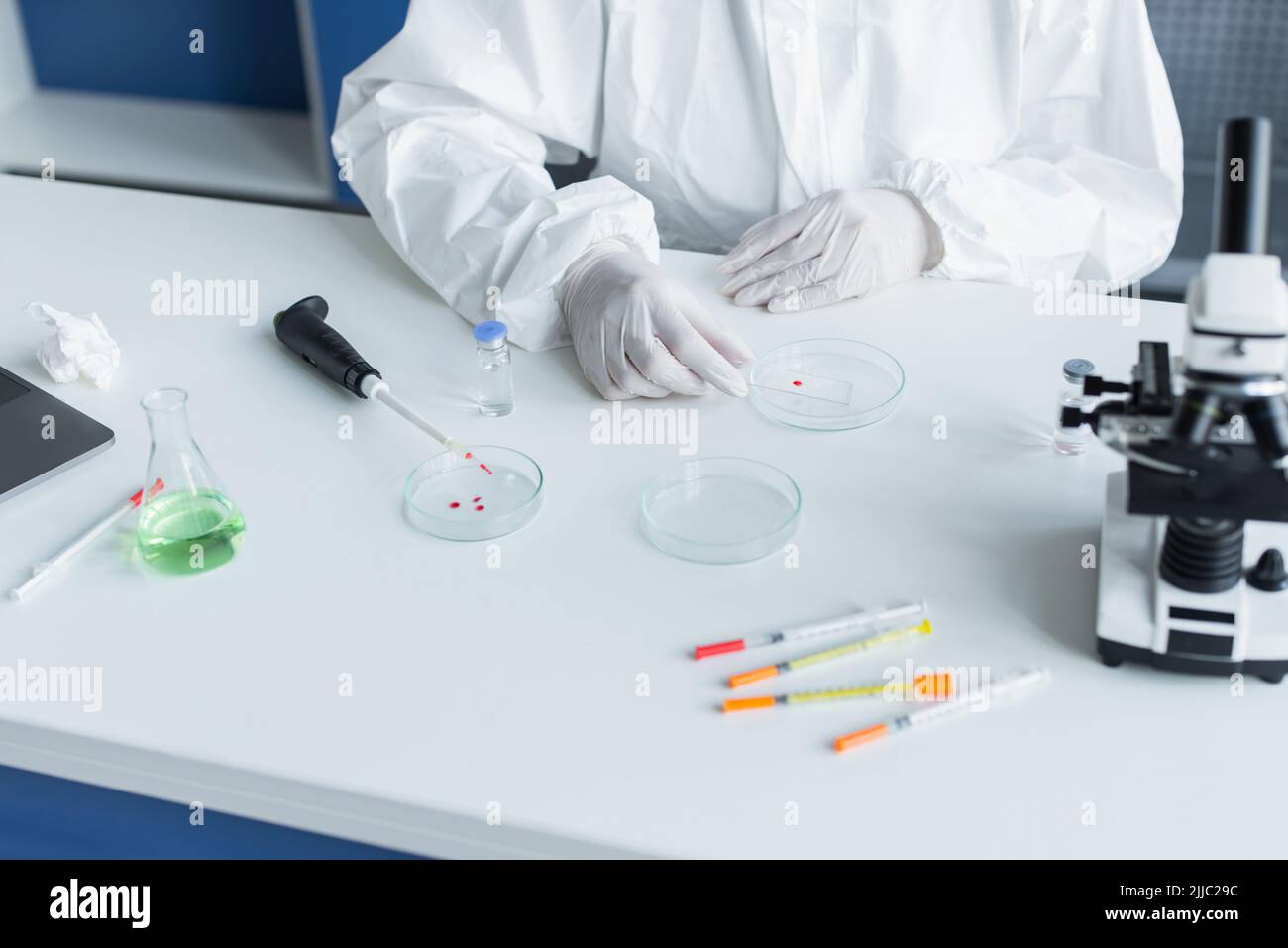 Cropped view of scientist in hazmat suit holding glass near petri ...
