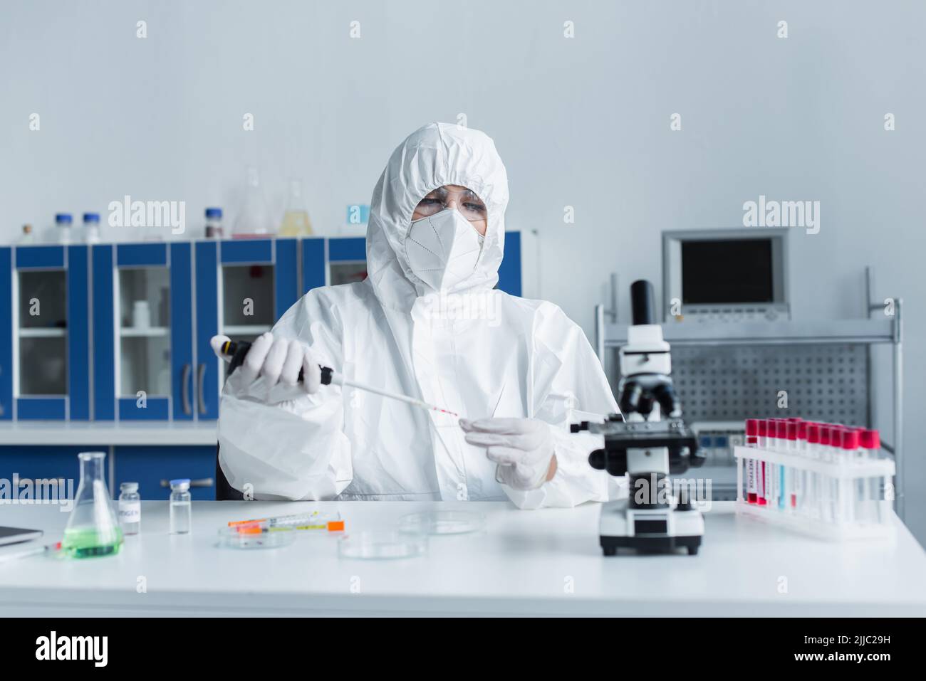 Scientist in hazmat suit working with pipette and glass near test tubes ...