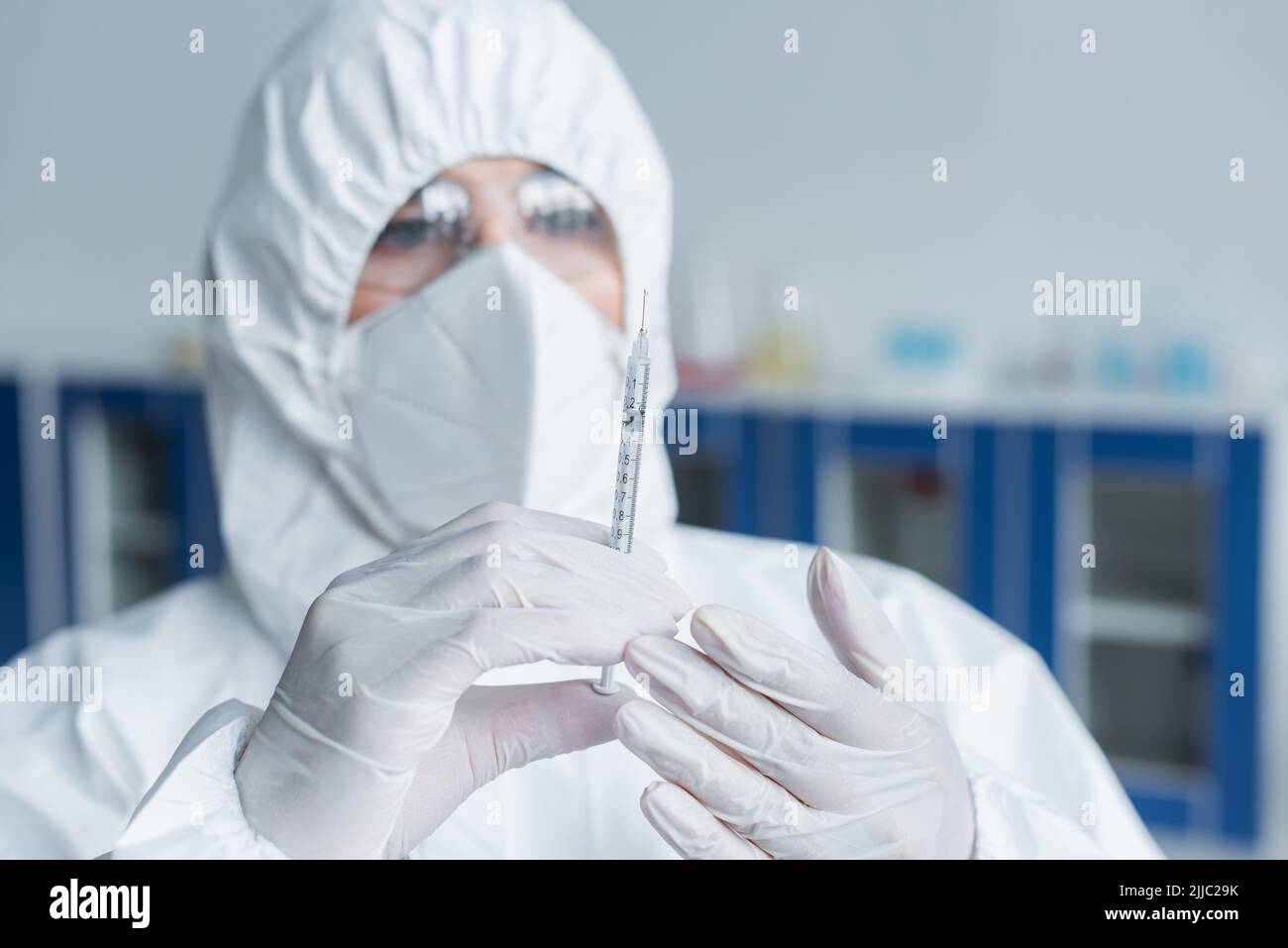 Blurred scientist in hazmat suit holding syringe in laboratory Stock ...