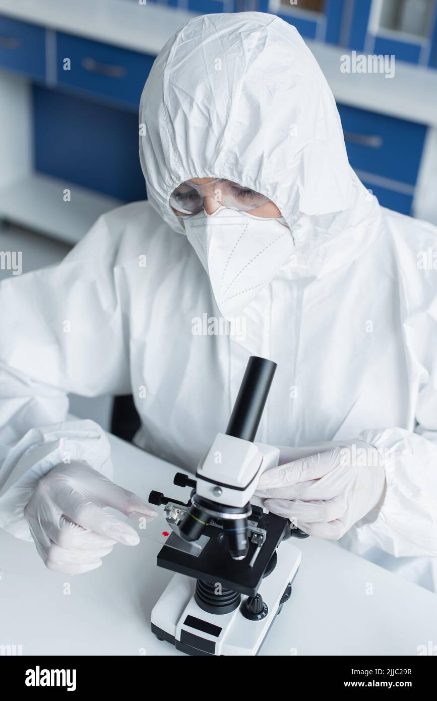 Scientist in hazmat suit holding glass near microscope in lab Stock ...