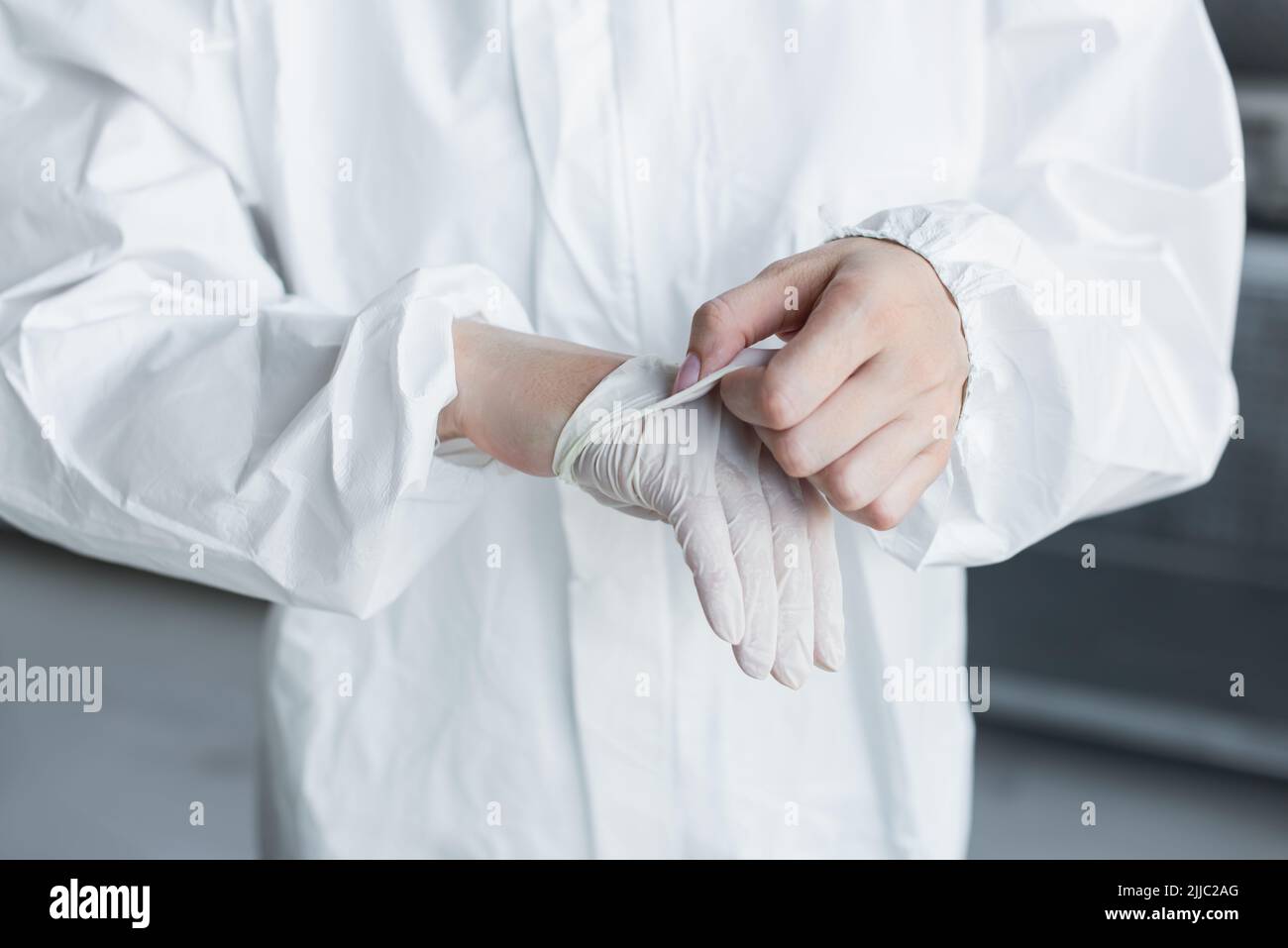 Cropped view of scientist in hazmat suit taking off latex glove in lab ...