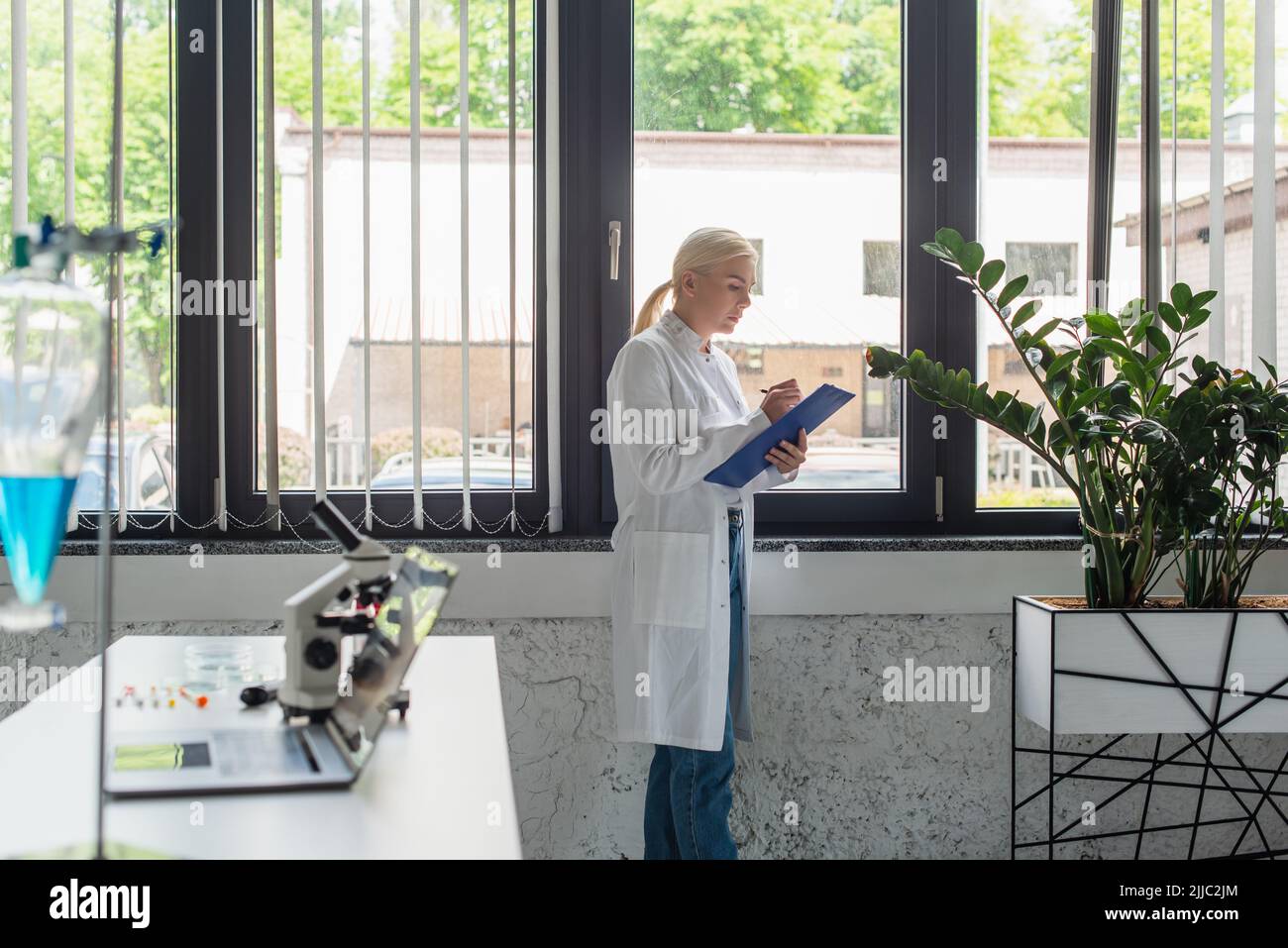 Side view of scientist writing on clipboard near window in laboratory ...