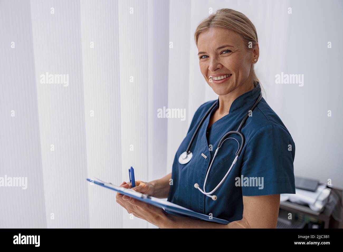 Professional woman doctor taking notes on clipboard and looking camera ...
