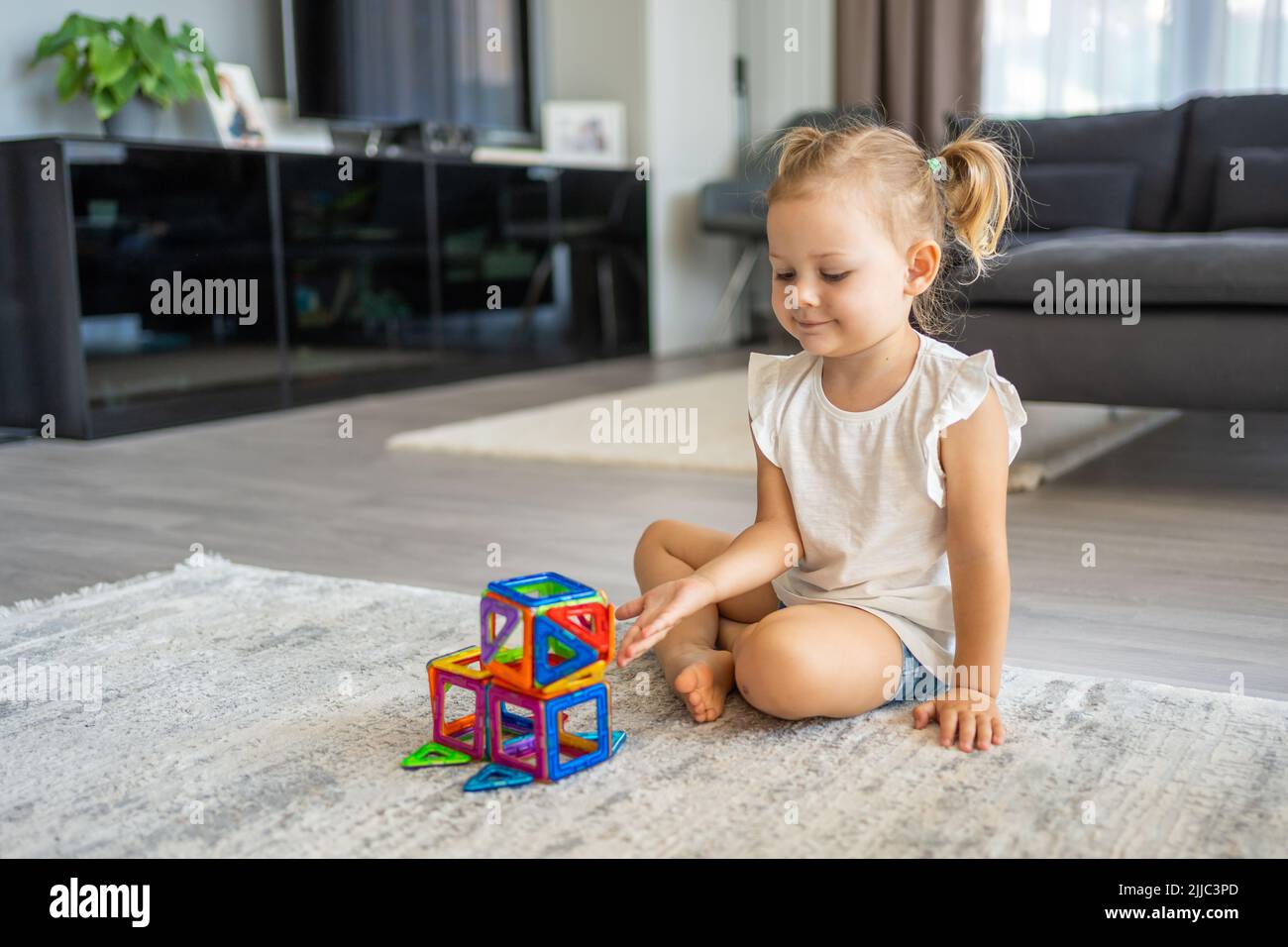 Little girl playing colorful magnet plastic blocks kit at home. The ...