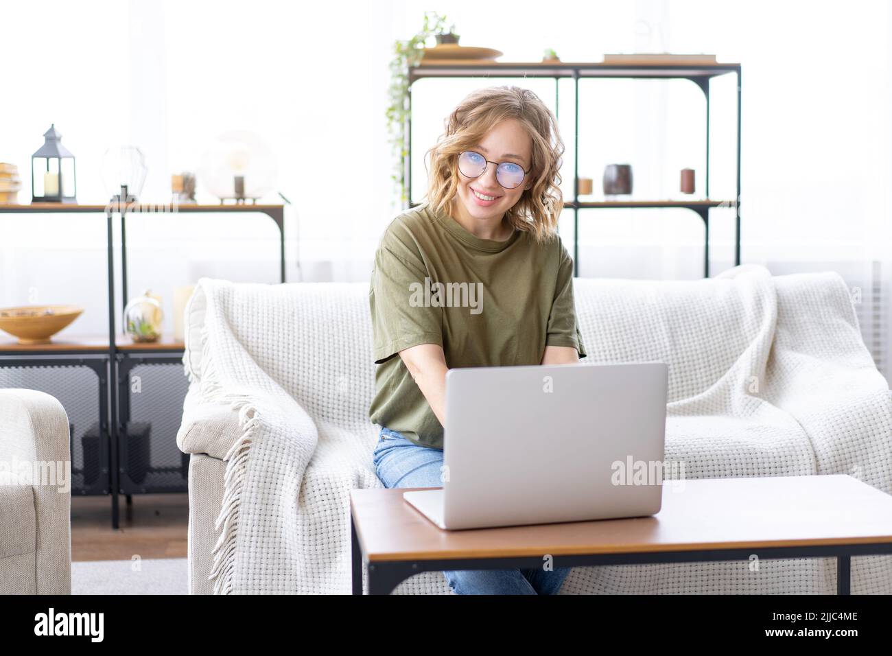 Woman with glasses use laptop typing keyboard sitting couch big window background home interior ...