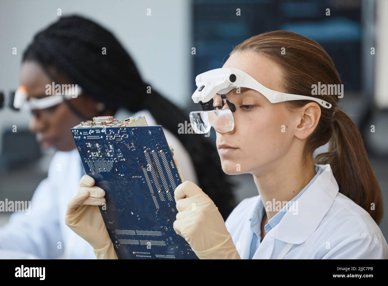 Side view portrait of young female engineer inspecting computer parts at quality control line ...