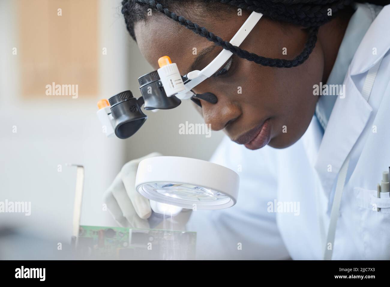 Close up portrait of black female engineer inspecting computer parts with magnifier at quality ...