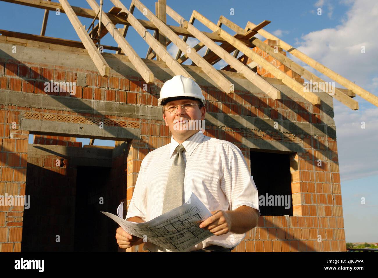 Civil engineer standing with building plans in front of unfinished ...