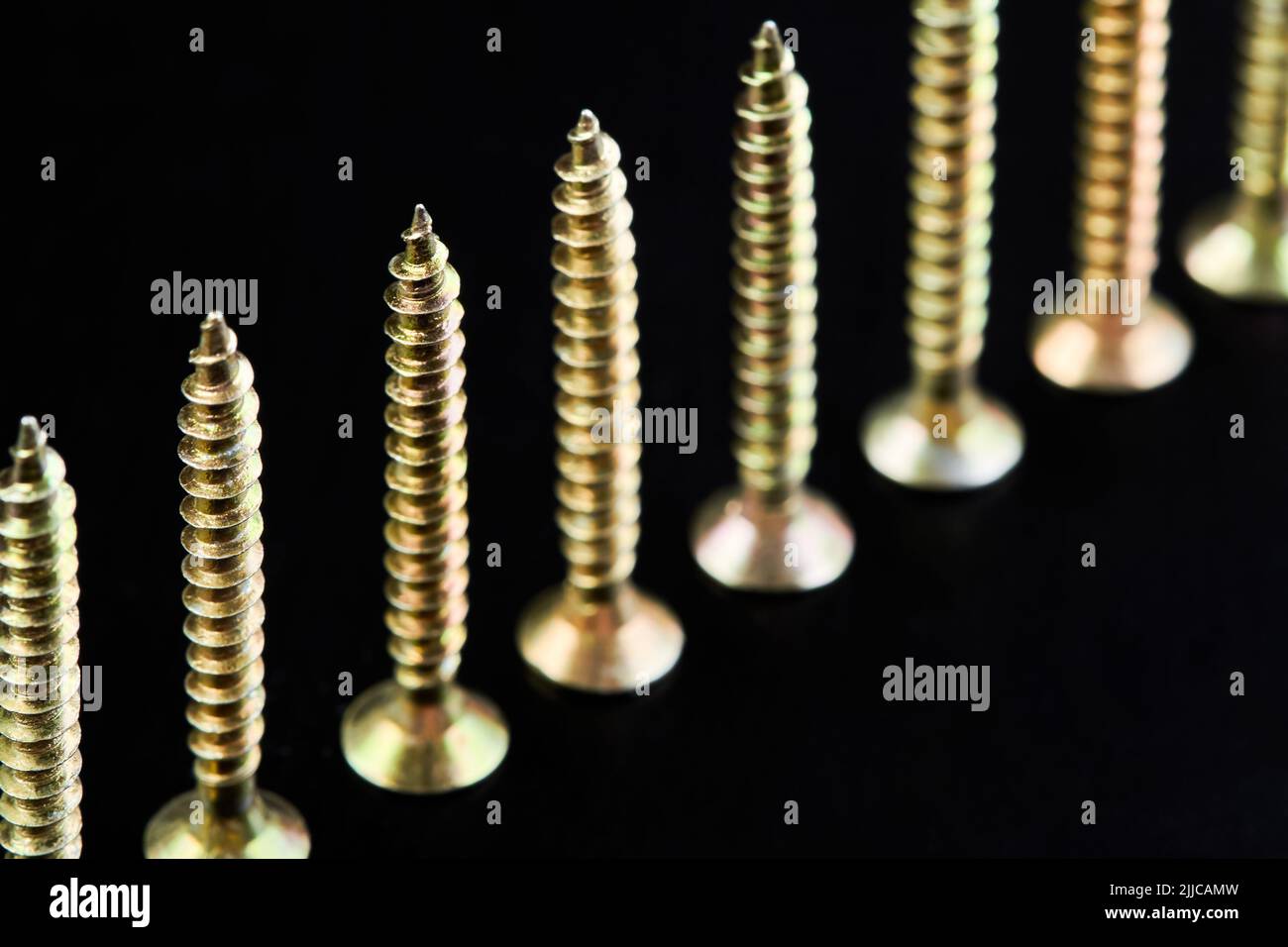 A row of screws or self-tapping screws with a yellow coating on a black ...
