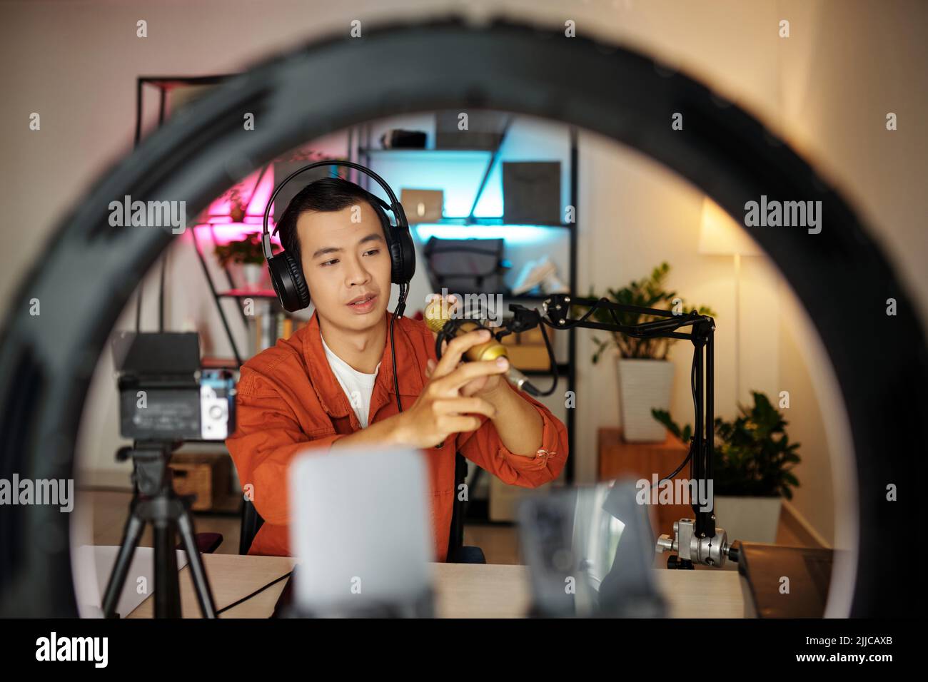 Portrait of young Asian streamer in headphones checking microphone to ...