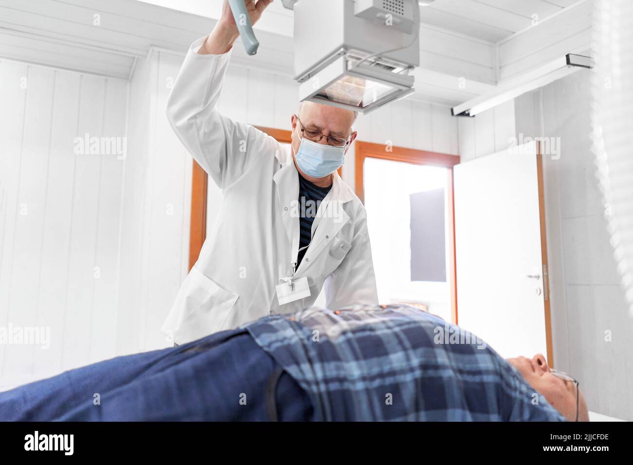 Doctor using a x-ray machine with a patient lying on a hospital room ...