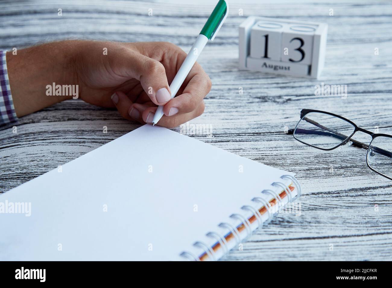 Man uses his left hand to wright in a notebook close up. Glasess and ...