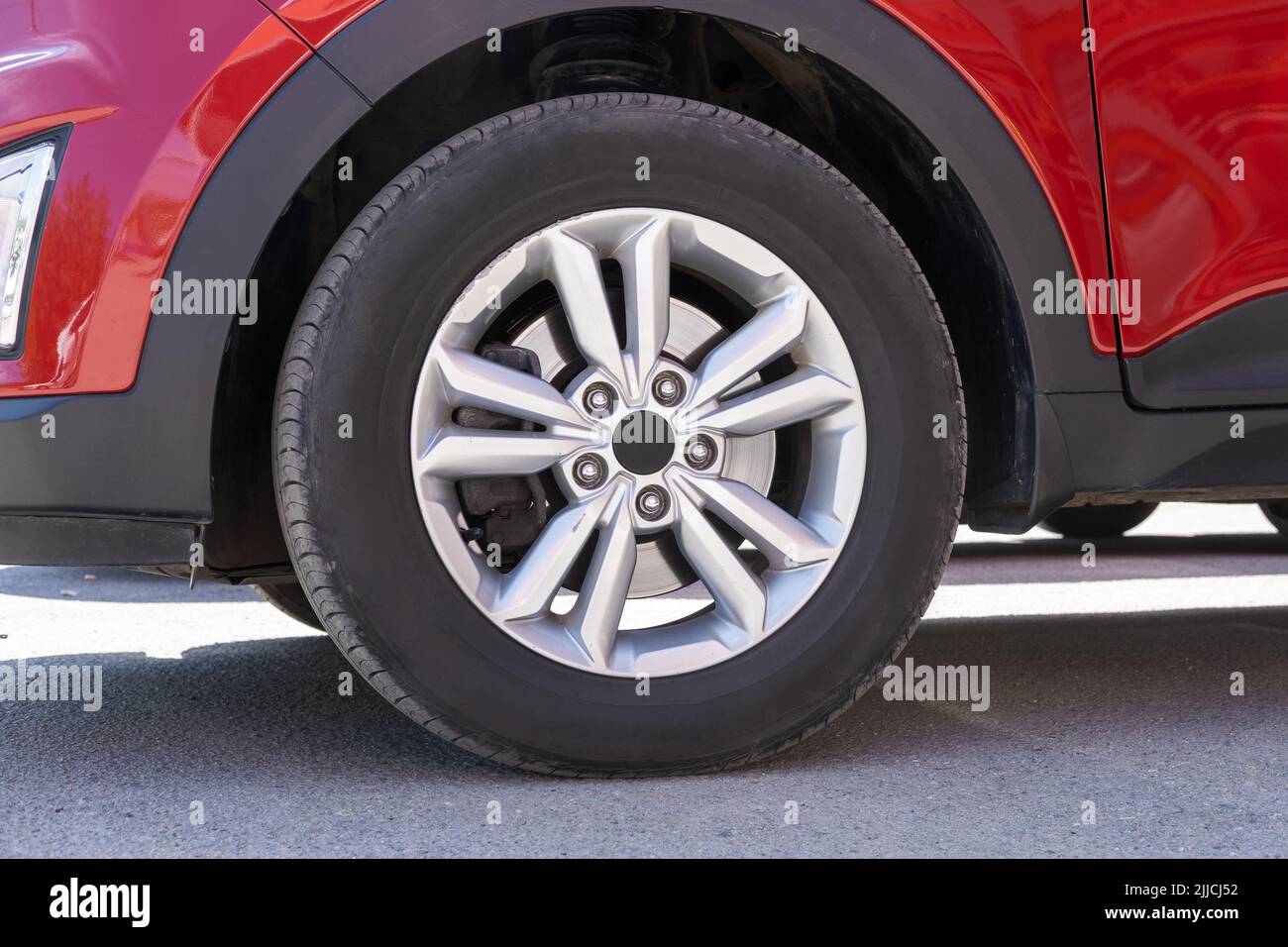 Fragment of red modern car with wheel on steel disc, close-up. Part of ...
