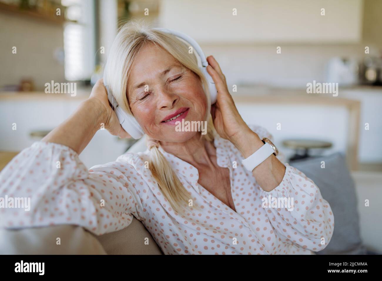Senior woman with headphones listening to relaxation music at home ...