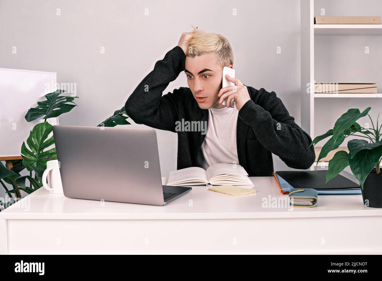 Young, frustrated, shocked man holds on to his head staring at a laptop ...