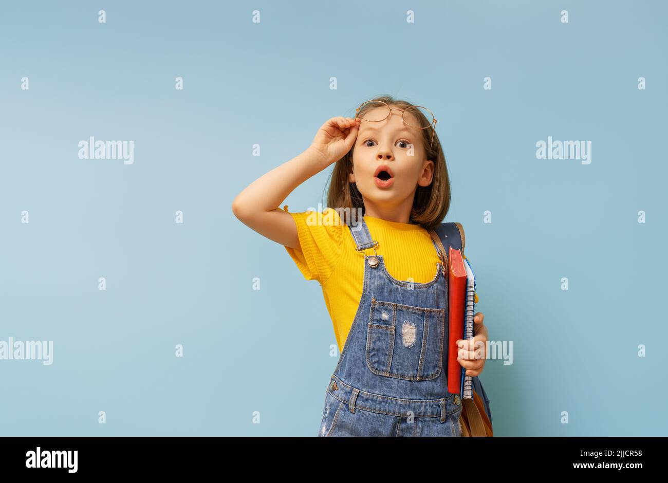 Cute happy kid standing on light blue background. Child with backpack ...