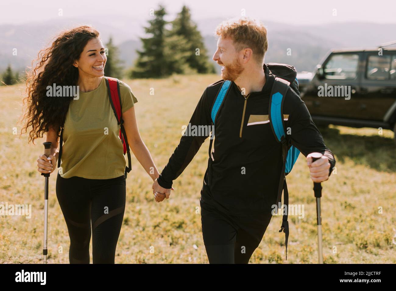 Smiling young couple starting walking with backpacks over green hills ...