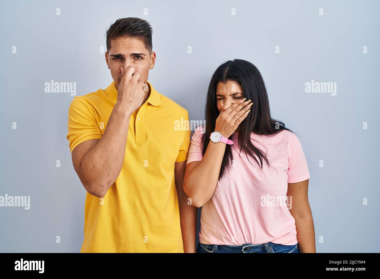 Young couple standing over isolated background smelling something ...