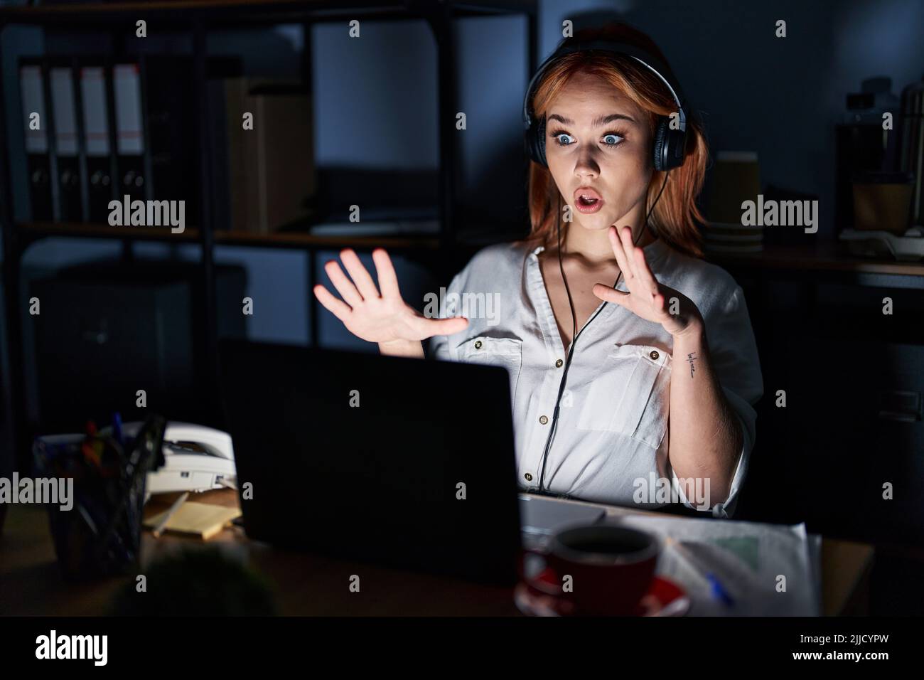 Young caucasian woman working at the office at night afraid and ...