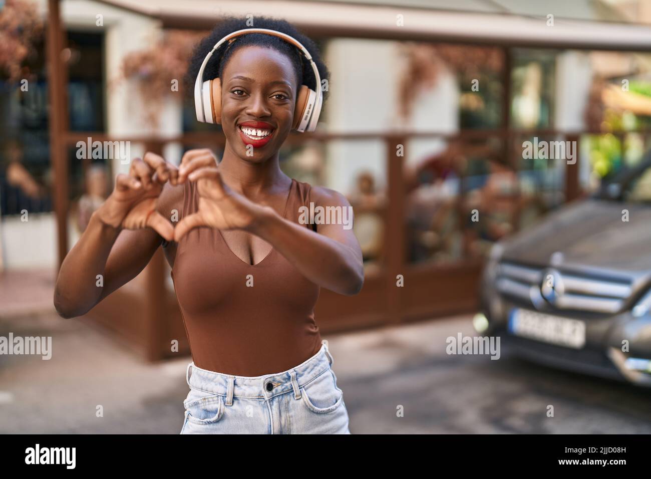 African woman with curly hair outdoors at the city wearing headphones ...