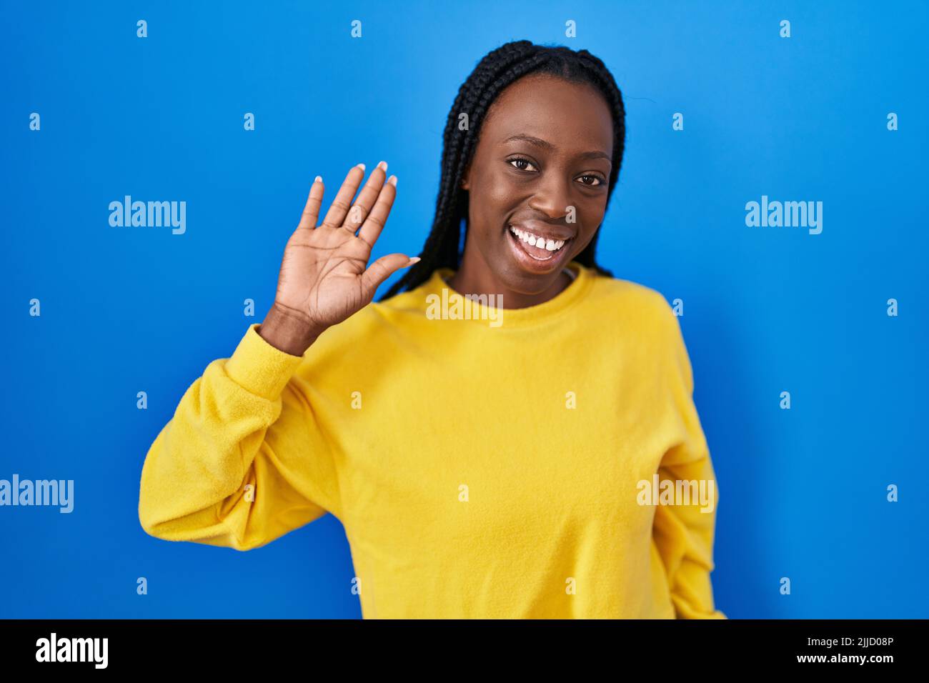 Beautiful black woman standing over blue background waiving saying ...