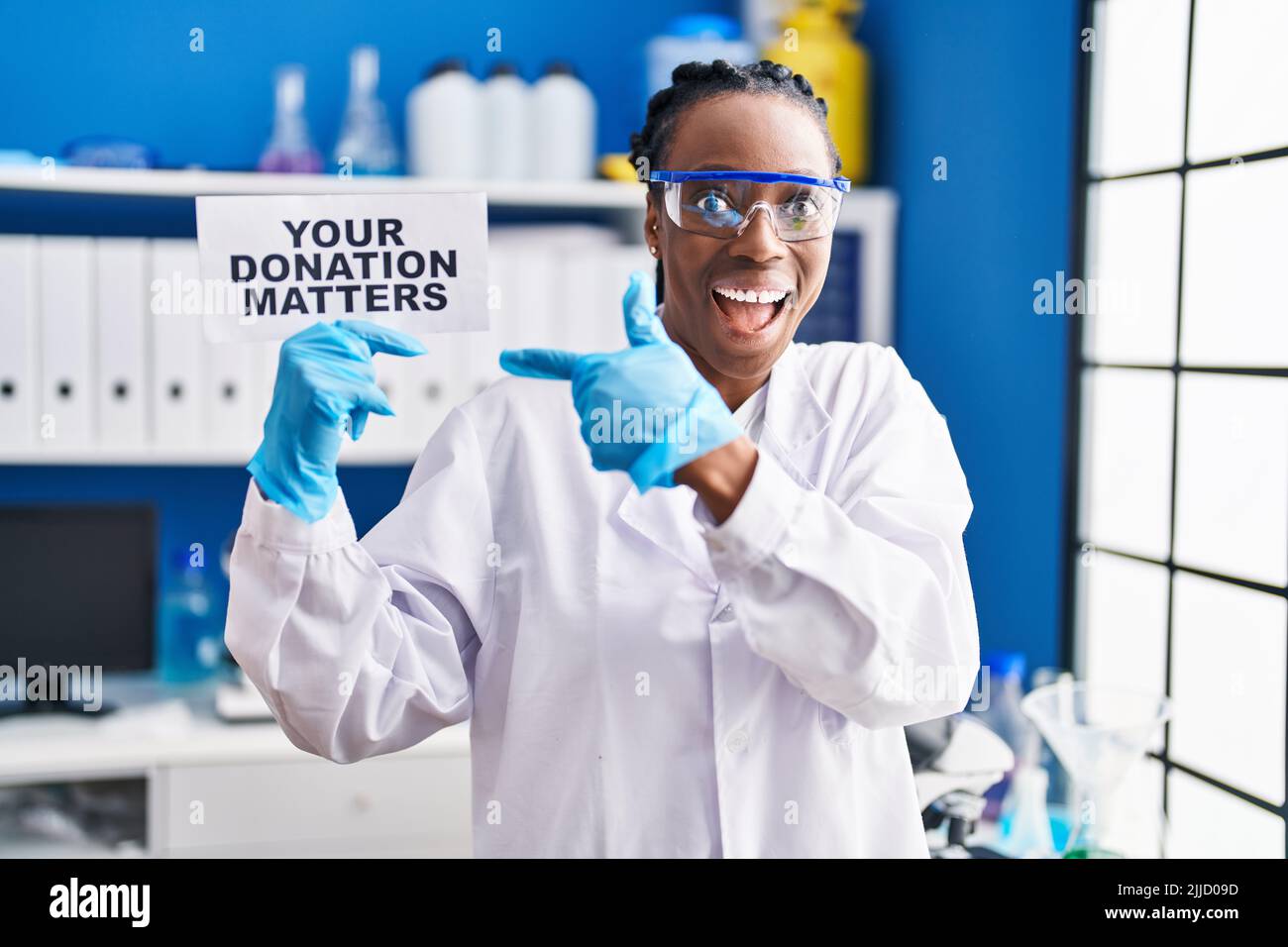 Beautiful black woman working at scientist laboratory holding your donation matters banner ...