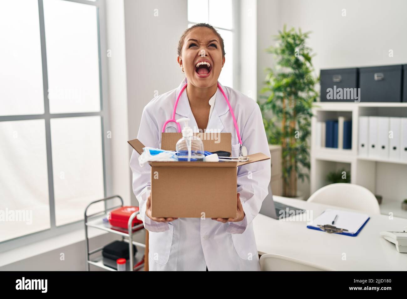 Young hispanic doctor holding box with medical items angry and mad ...