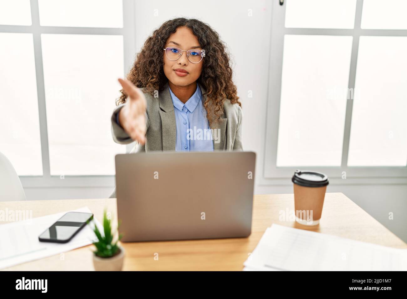 Beautiful hispanic business woman sitting on desk at office working ...