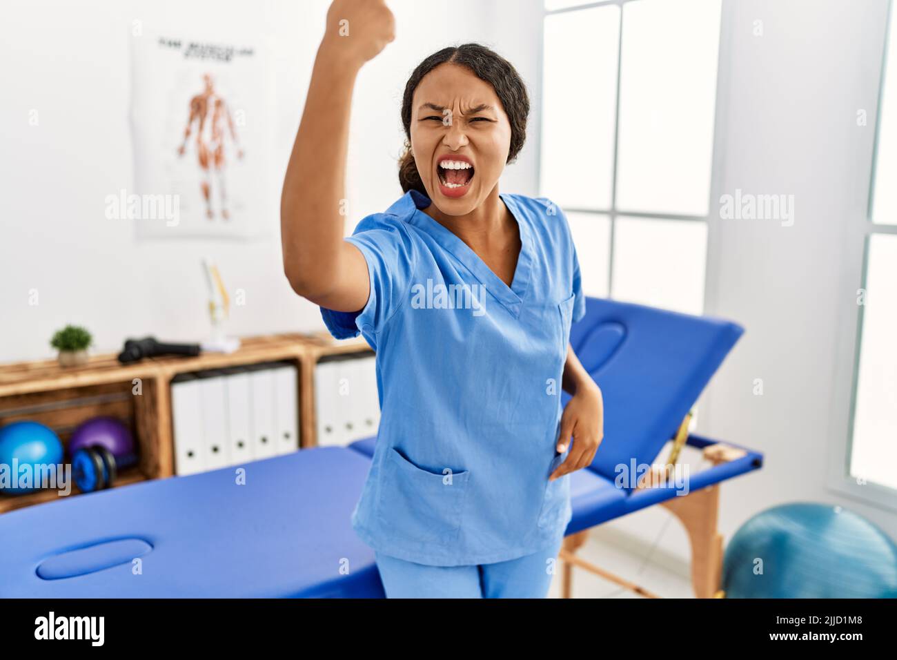 Beautiful hispanic physiotherapist woman at pain recovery clinic angry ...