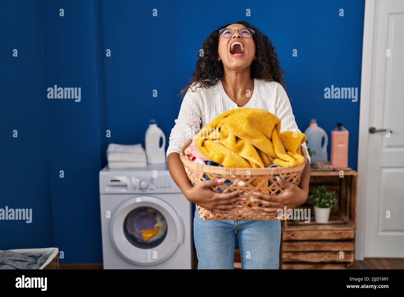 Young hispanic woman doing laundry holding wicker basket angry and mad ...