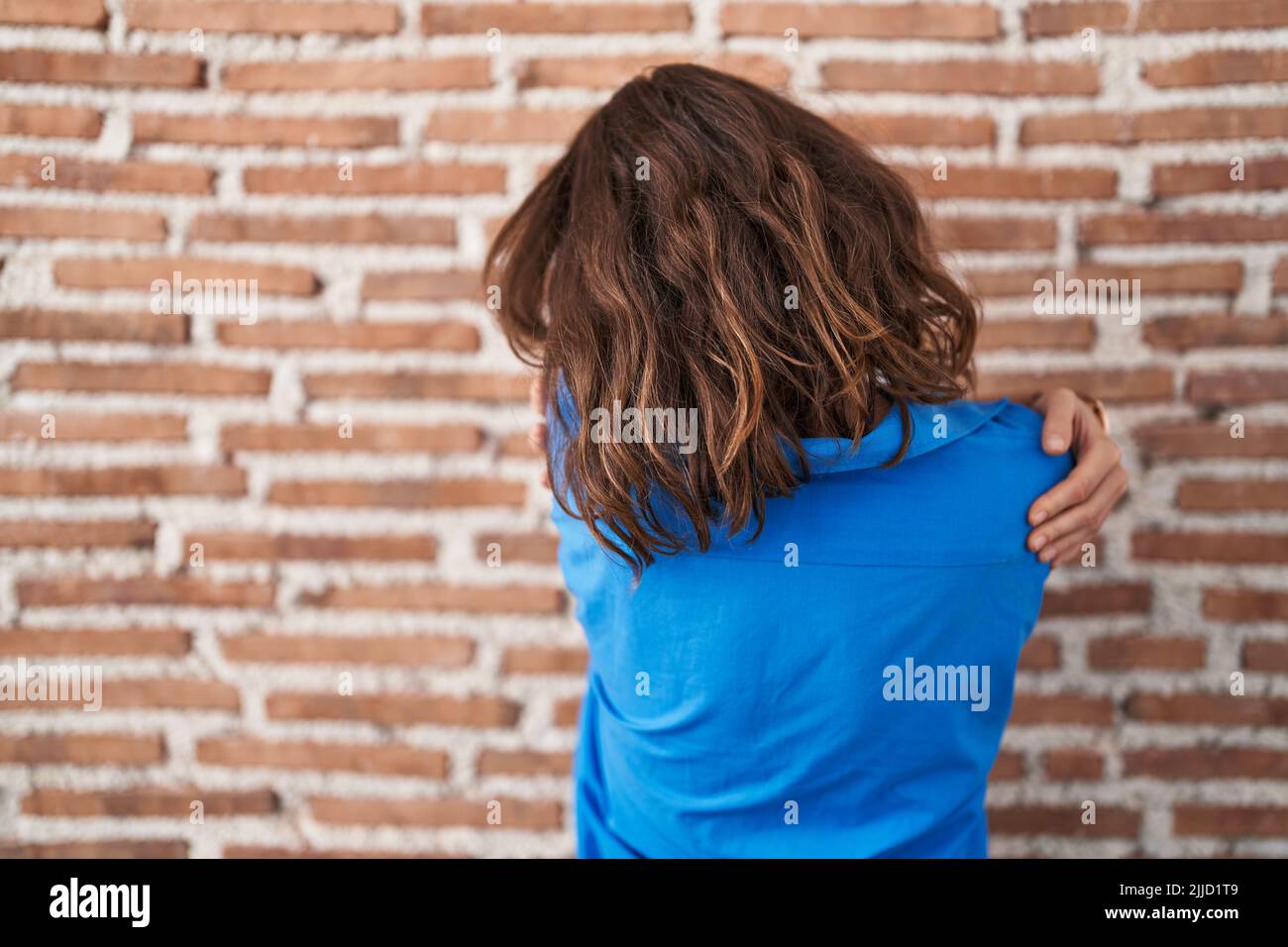 Beautiful brunette woman standing over bricks wall hugging oneself ...