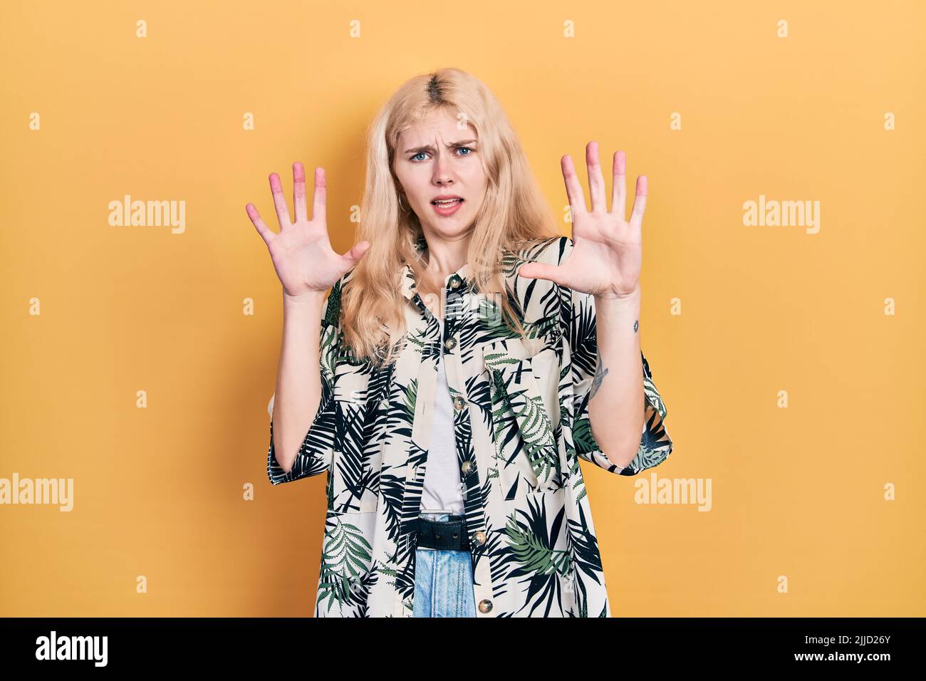 Beautiful caucasian woman with blond hair wearing tropical shirt afraid ...