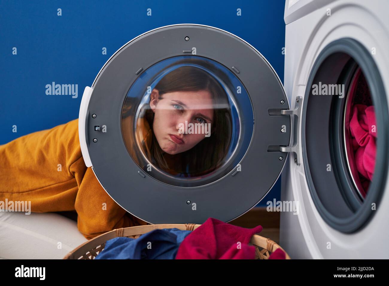Young brunette woman looking through the washing machine window ...