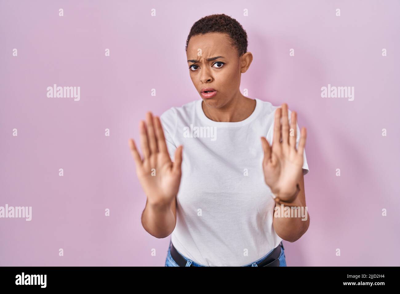 Beautiful african american woman standing over pink background moving ...