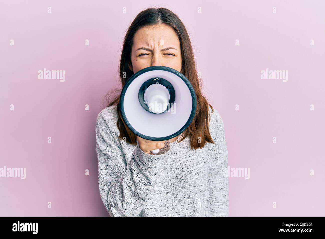 Young brunette woman shouting and screaming through megaphone over pink ...