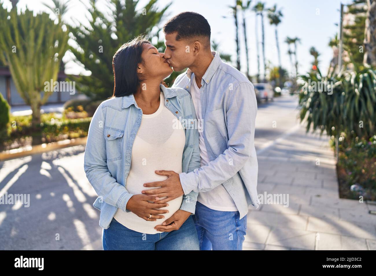 Young latin couple expecting baby touching belly and kissing at park Stock Photo - Alamy