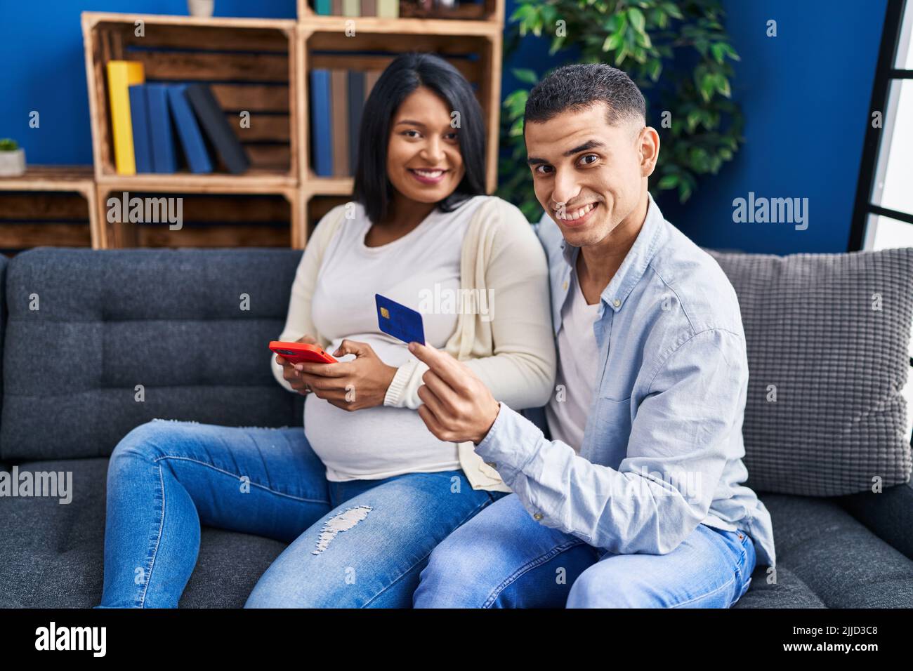 Young latin couple expecting baby using smartphone and credit card at ...