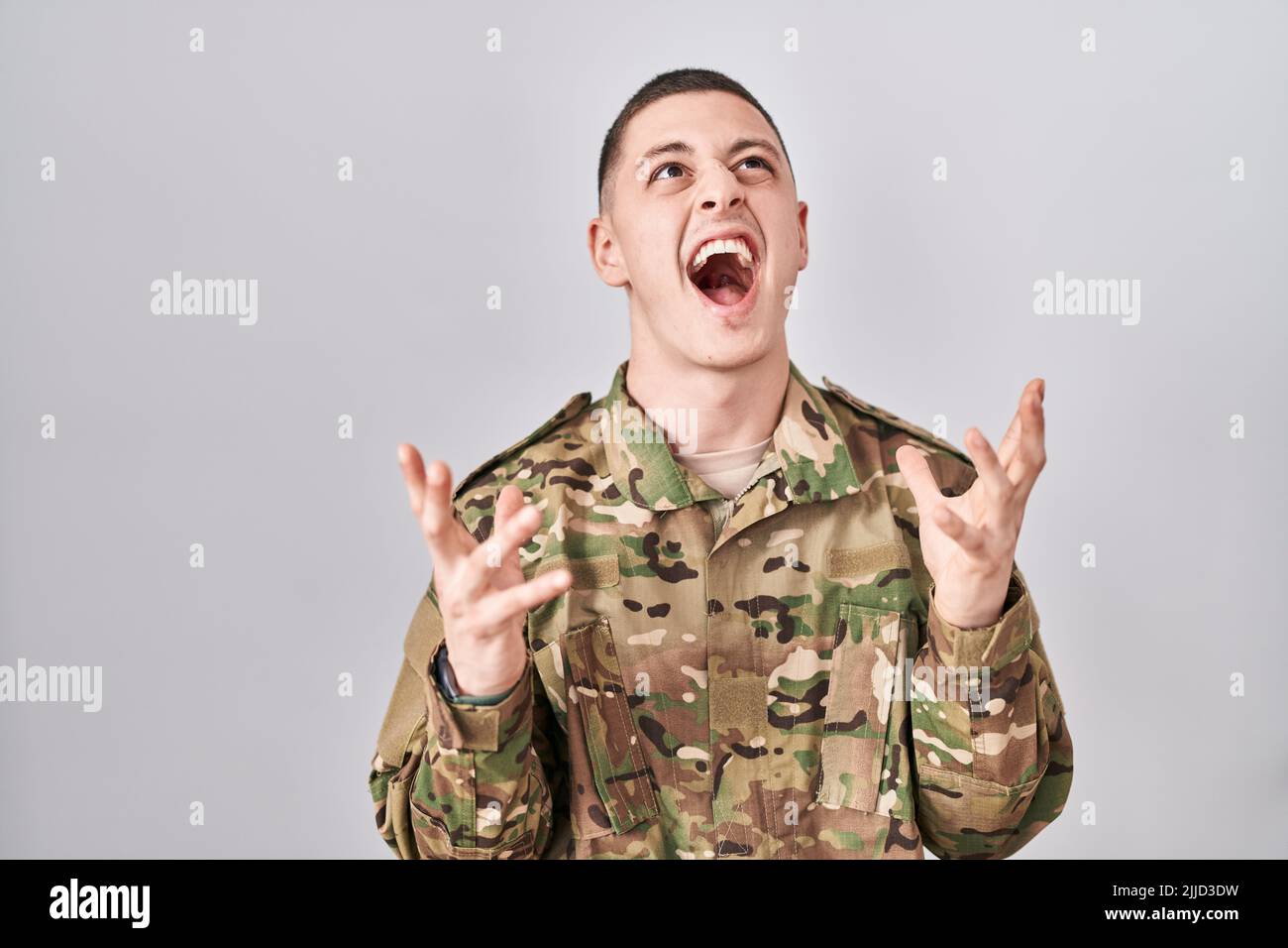 Young man wearing camouflage army uniform crazy and mad shouting and ...