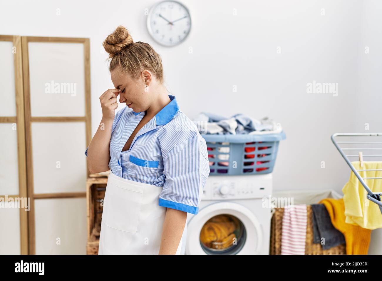 Young caucasian woman wearing cleaner uniform at the laundry room tired rubbing nose and eyes ...
