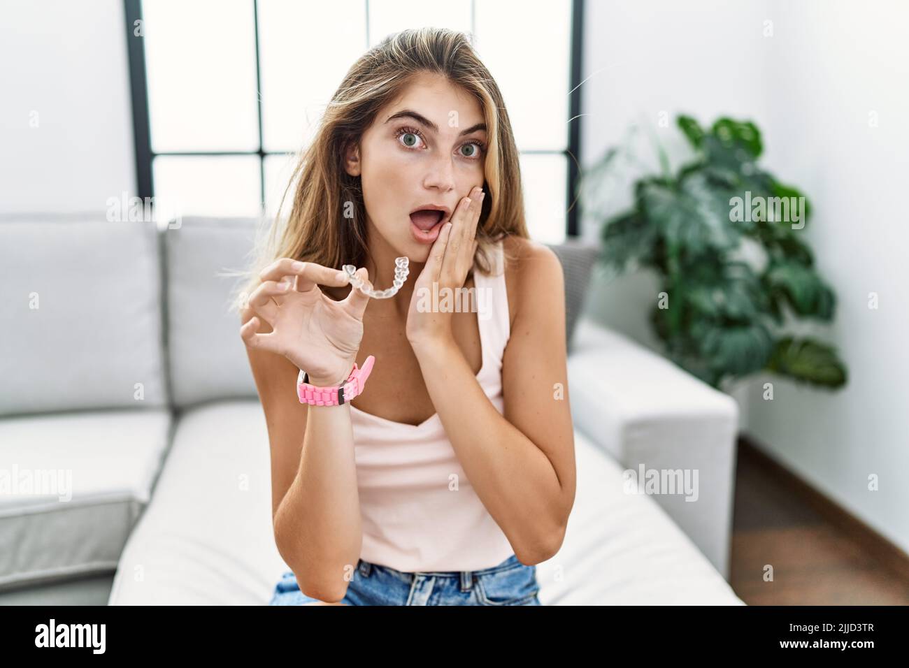 Young blonde woman holding invisible aligner orthodontic afraid and ...
