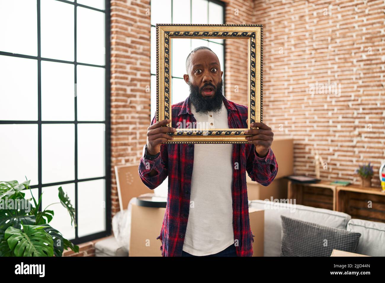 African american man putting face in empty frame in shock face, looking ...