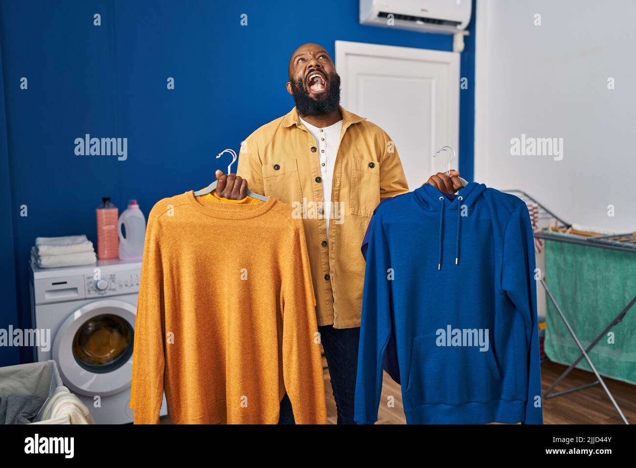 African american man holding clean clothes on hangers at laundry room ...