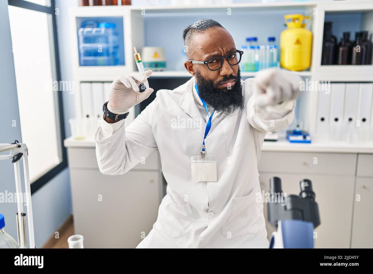 African american man working at scientist laboratory holding syringe pointing with finger to the ...