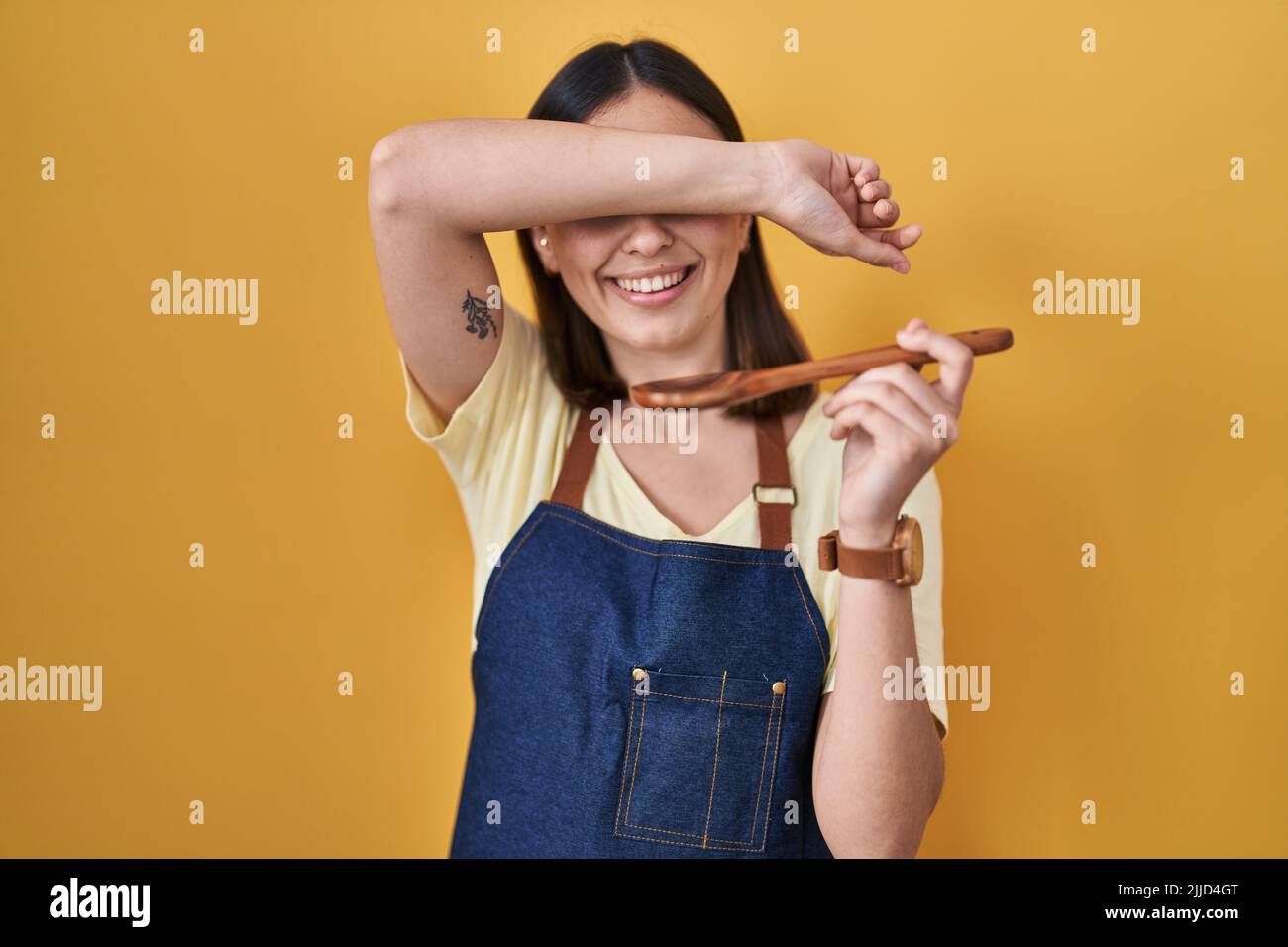 Hispanic girl eating healthy wooden spoon smiling cheerful playing peek ...