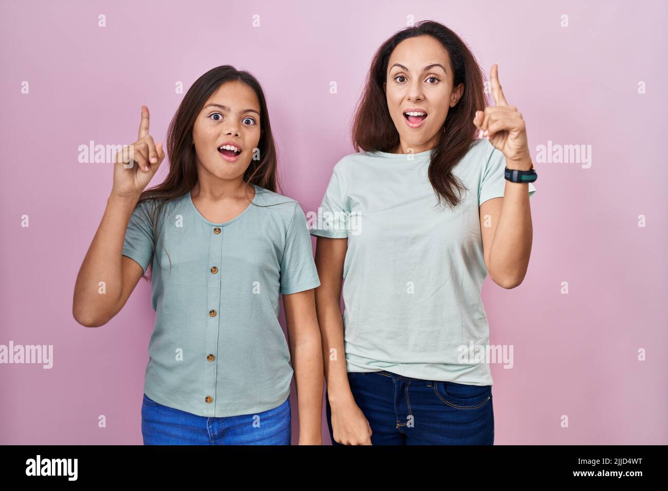 Young Mother And Daughter Standing Over Pink Background Pointing Finger