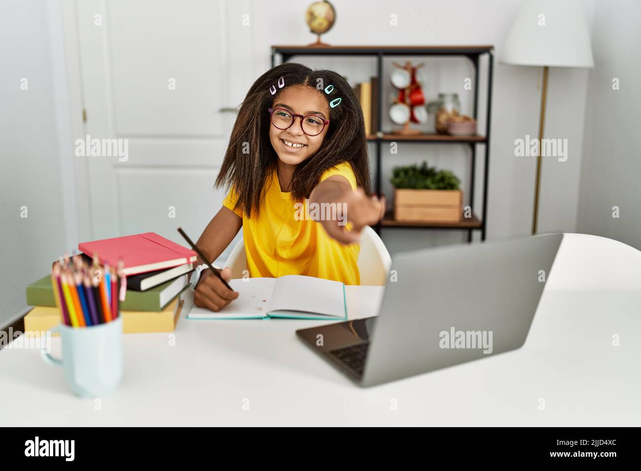 Young african american girl doing homework at home pointing to you and ...