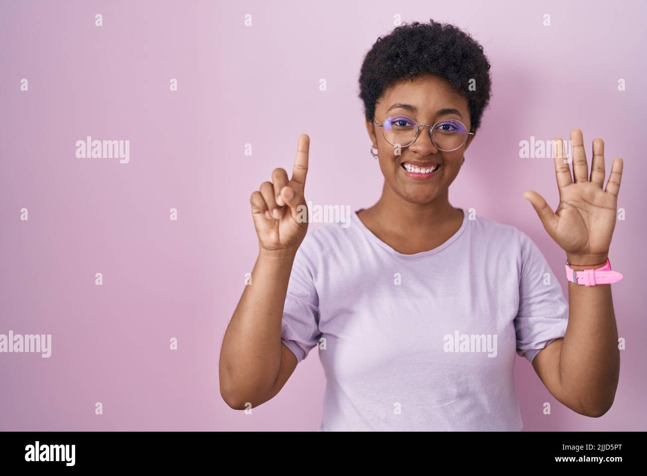 Young african american woman standing over pink background showing and ...