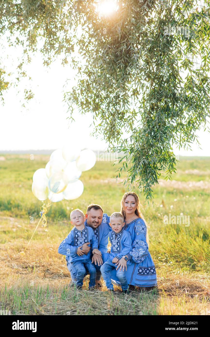 Happy parents with two their twins sons sit on grass and rest on meadow ...